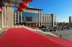 Um edifício moderno com tapete vermelho que leva a uma entrada com portão, um estacionamento e lanternas vermelhas.