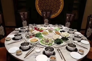 Mesa de jantar redonda com diversos pratos e tigelas, cercada por cadeiras.