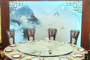 Mesa redonda com tampo de mármore branco, rodeada por cadeiras com estampas florais, com um tradicional quadro chinês ao fundo.