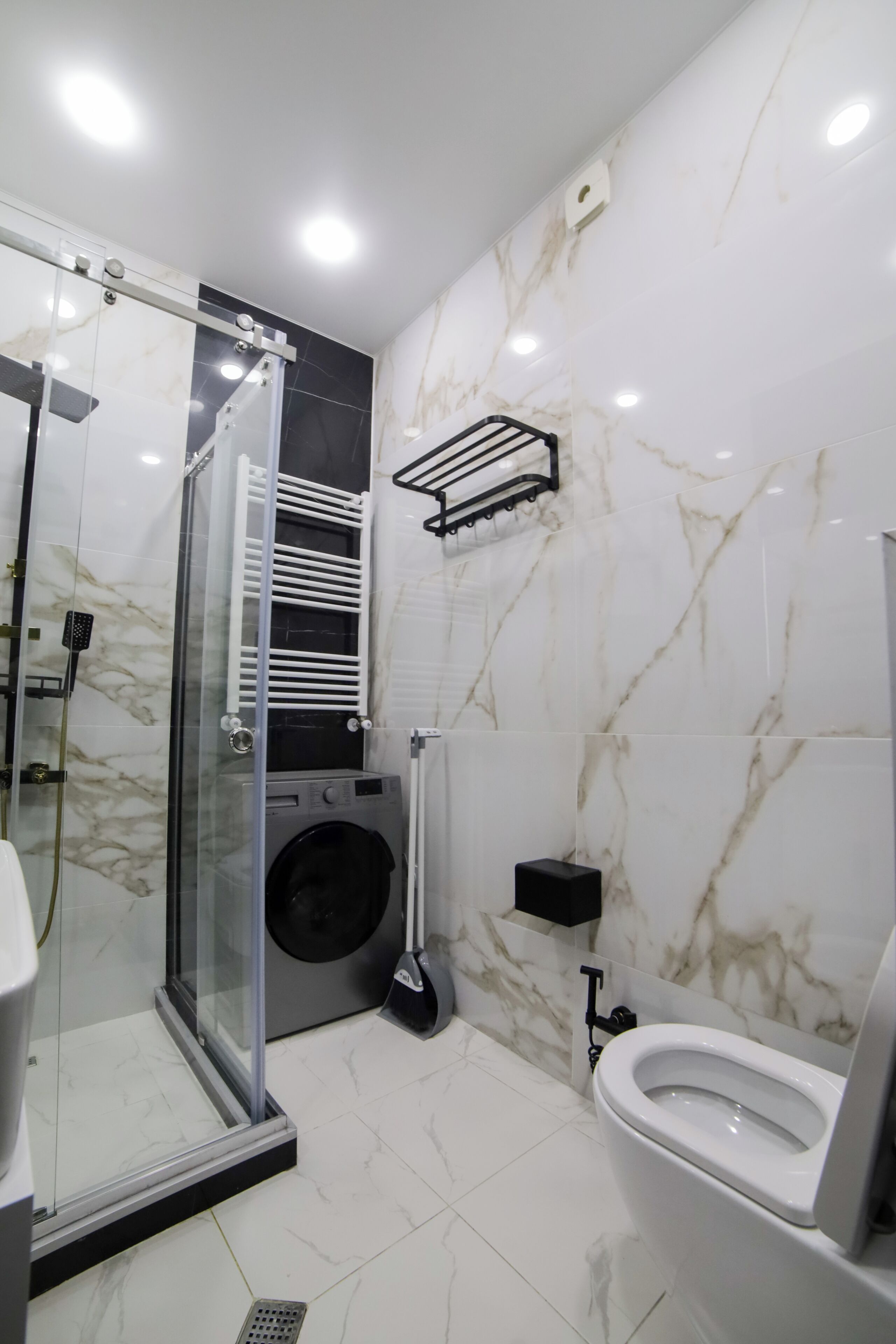 Uma casa de banho moderna com cabine de duche em vidro, máquina de lavar integrada, sanita e porta-toalhas.