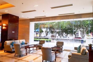 Um saguão de hotel com área de estar, janelas amplas e vista para a rua.
