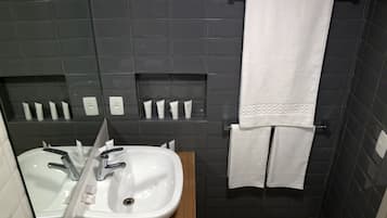 Uma casa de banho com uma pia branca, duas torneiras, um espelho e um porta-toalhas com duas toalhas.