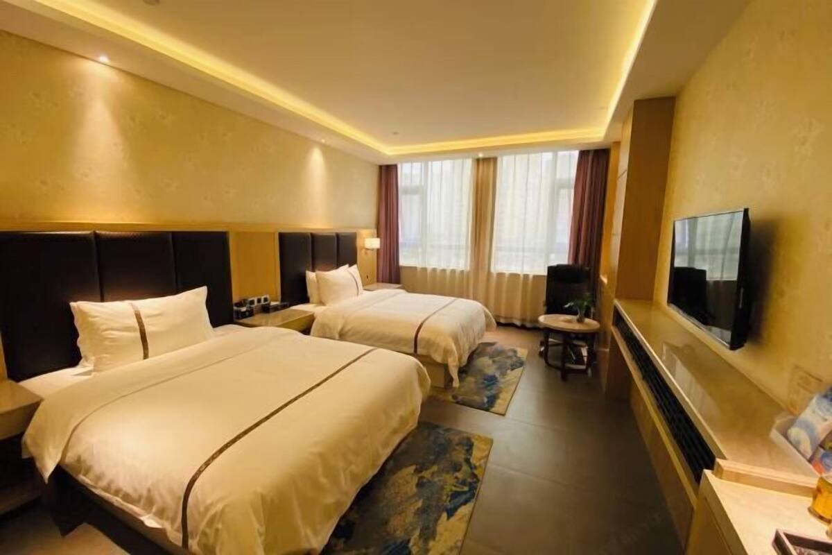 Quarto de hotel com duas camas, televisão, secretária e janela com cortinas.