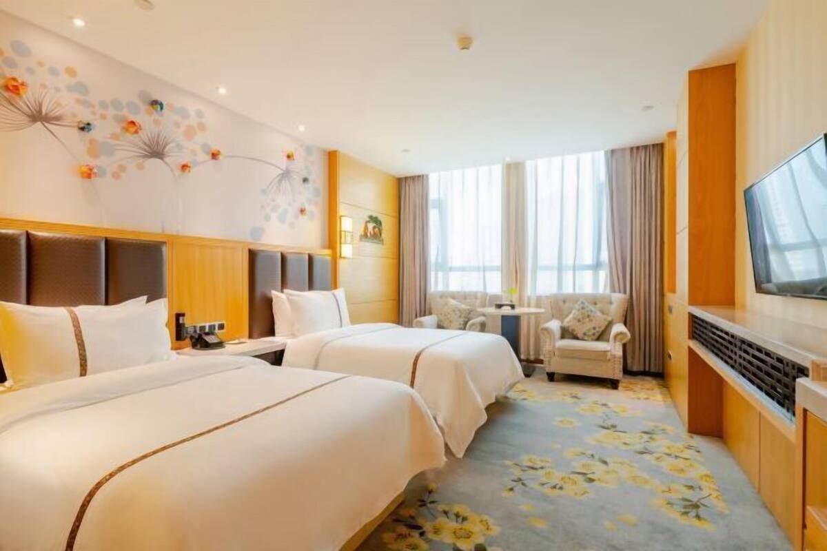 Quarto de hotel com duas camas, televisão, escrivaninha e janela com cortinas.