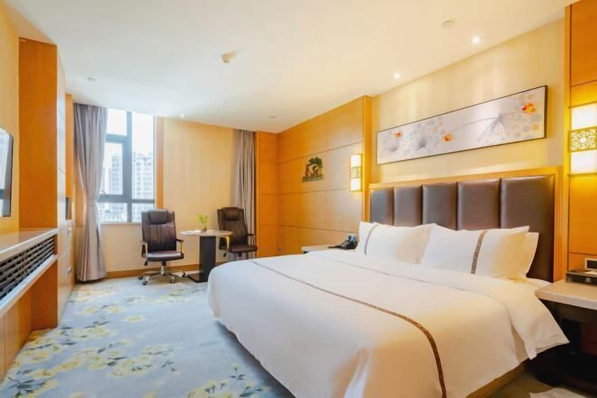 Quarto de hotel com uma cama grande, uma escrivaninha, uma cadeira e uma televisão.
