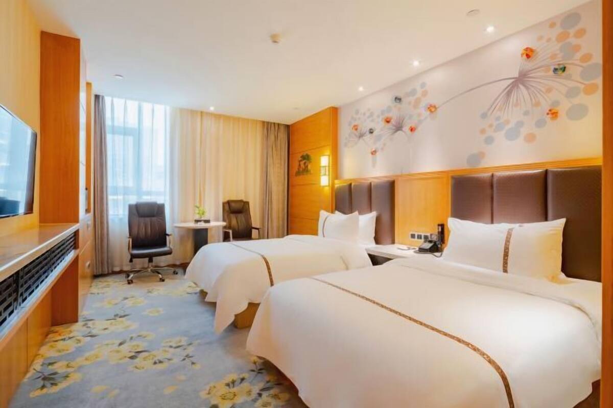 Quarto de hotel com duas camas, uma escrivaninha, uma cadeira, uma televisão e um tapete estampado com flores.