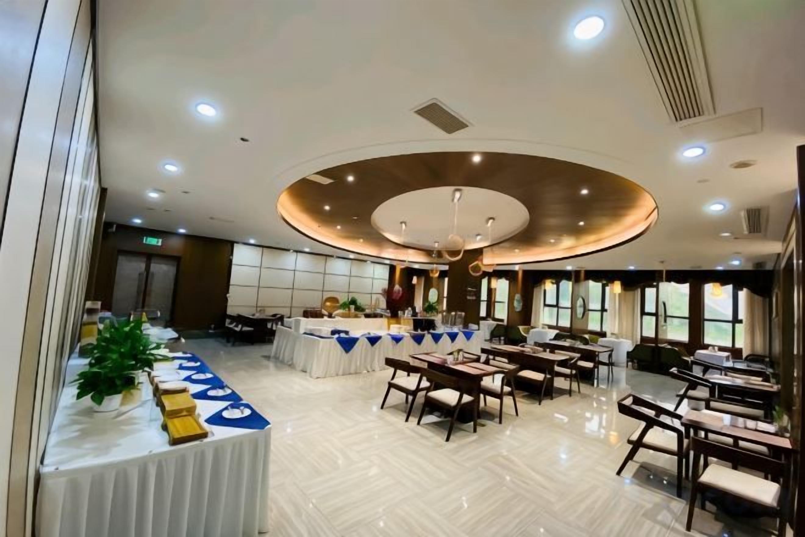 Um hall de hotel espaçoso com uma mesa redonda central, várias mesas de jantar e um balcão de recepção.