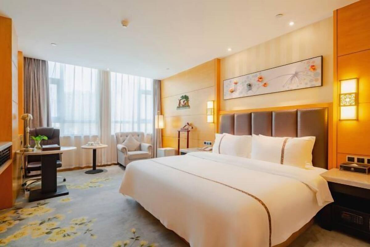 Quarto de hotel com uma cama grande, uma escrivaninha, uma cadeira e uma mesinha.