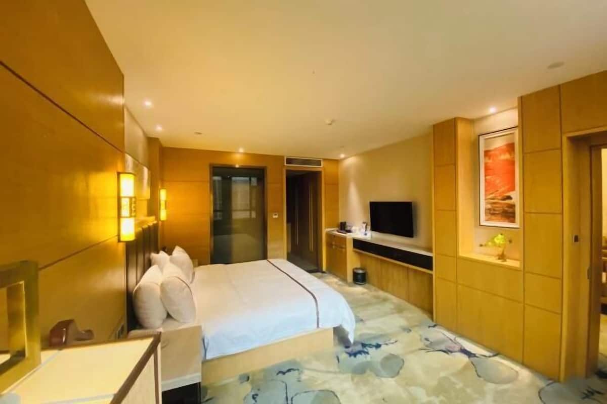Quarto de hotel com cama, televisão, escrivaninha e porta de banheiro.