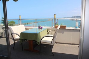 Uma varanda com mesa e cadeiras, com vista para uma área costeira e uma visão clara do mar, com uma ponte ao longe.