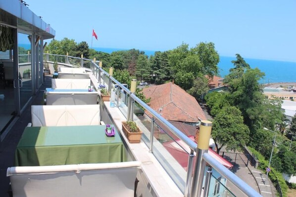Uma varanda com mesa e cadeiras, com vista para uma área costeira com árvores e edifícios.
