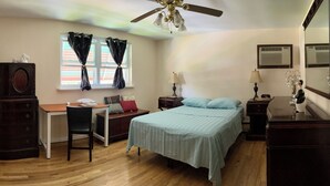 Quarto com cama, escrivaninha, cadeira, cômoda e ventilador de teto.