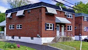 Um edifício de dois andares em tijolo, com entrada frontal, um pequeno alpendre e degraus que levam à porta principal.