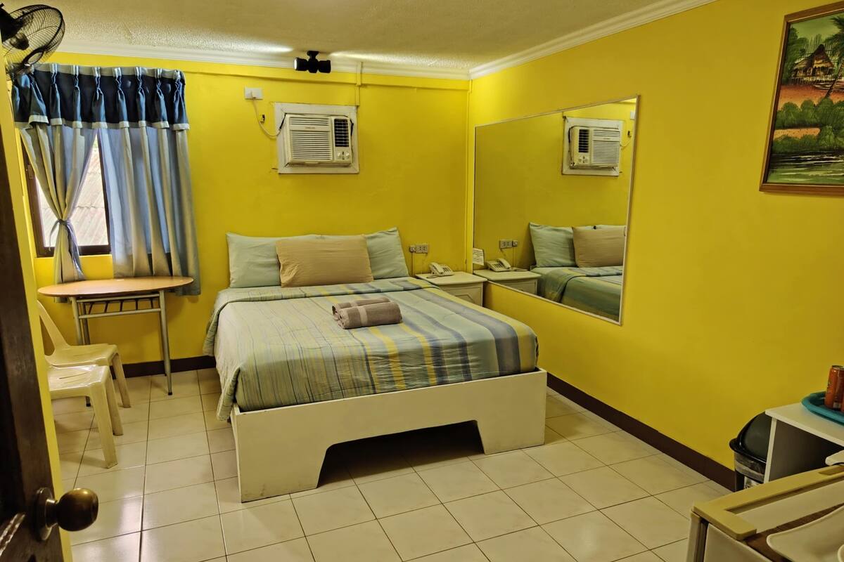 Quarto com cama, mesas de cabeceira, espelho, ar condicionado e janela com cortinas.