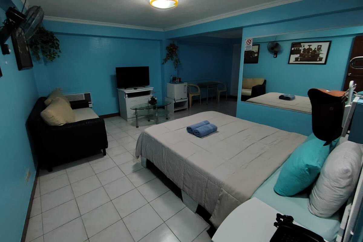 Quarto de hotel com uma cama, uma escrivaninha, televisão, cadeira e uma mesa pequena.