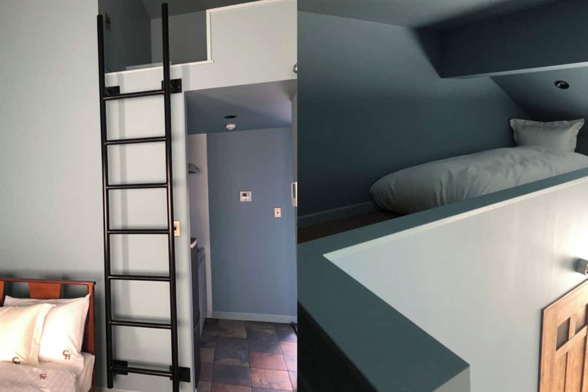 Quarto com cama, escada, porta e lance de escadas.
