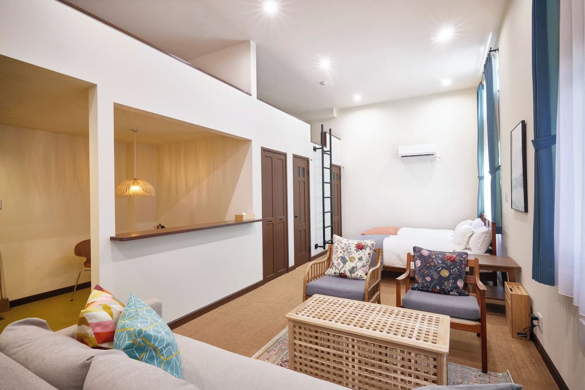 Uma sala de estar moderna com sofá, cadeiras, uma mesa pequena e uma cama com cabeceira.