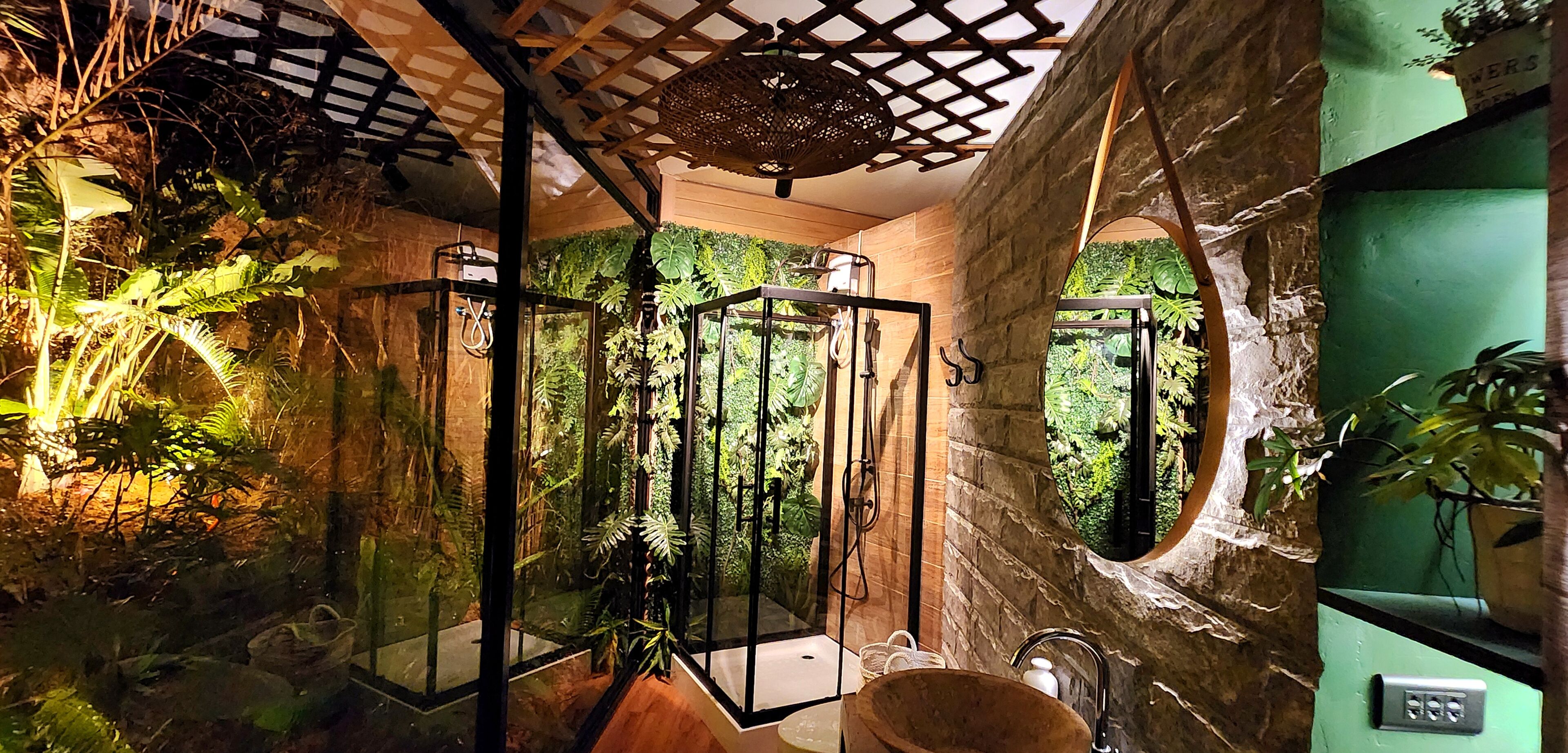 Casa de banho com cabine de vidro, lavatório de madeira e parede verde com plantas.
