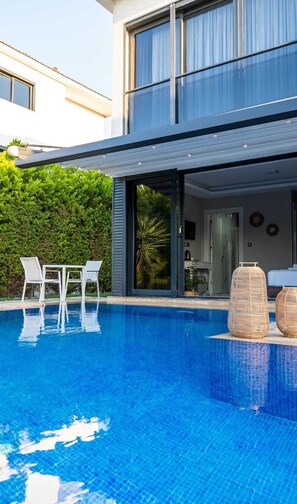 Uma casa moderna com piscina, área de estar externa e porta de vidro que dá para o interior.