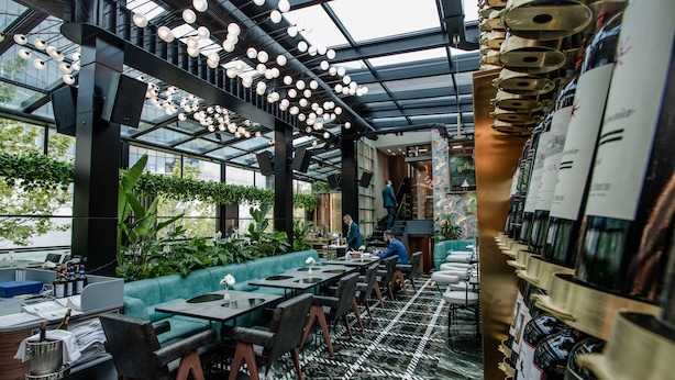Um restaurante moderno com um balcão extenso, assentos verdes e uma variedade de garrafas de vinho em exposição.