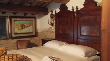 Quarto com cama de madeira, roupa de cama branca, cabeceira de madeira, pintura emoldurada e uma pequena mesa com abajur.