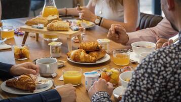 Disposição de café da manhã com croissants, suco de laranja e diversas opções para o café da manhã sobre uma mesa de madeira.