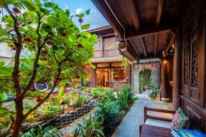 Um edifício de madeira com varanda coberta, um jardim com diversas plantas e um banco.