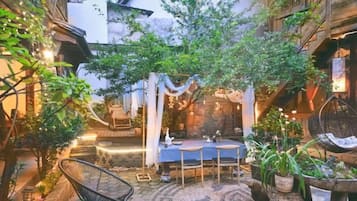 Pátio externo com mesa e cadeiras, cercado por vasos de plantas e um muro de pedra.