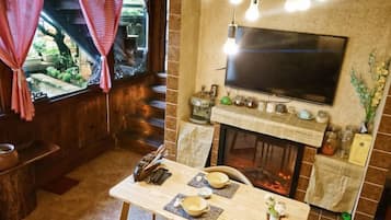 Um quarto aconchegante com lareira, TV fixada acima e uma mesa de jantar posta, com pratos e um vaso de flores.
