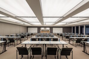 Sala de conferências com várias mesas e cadeiras, uma tela grande na frente e um projetor.