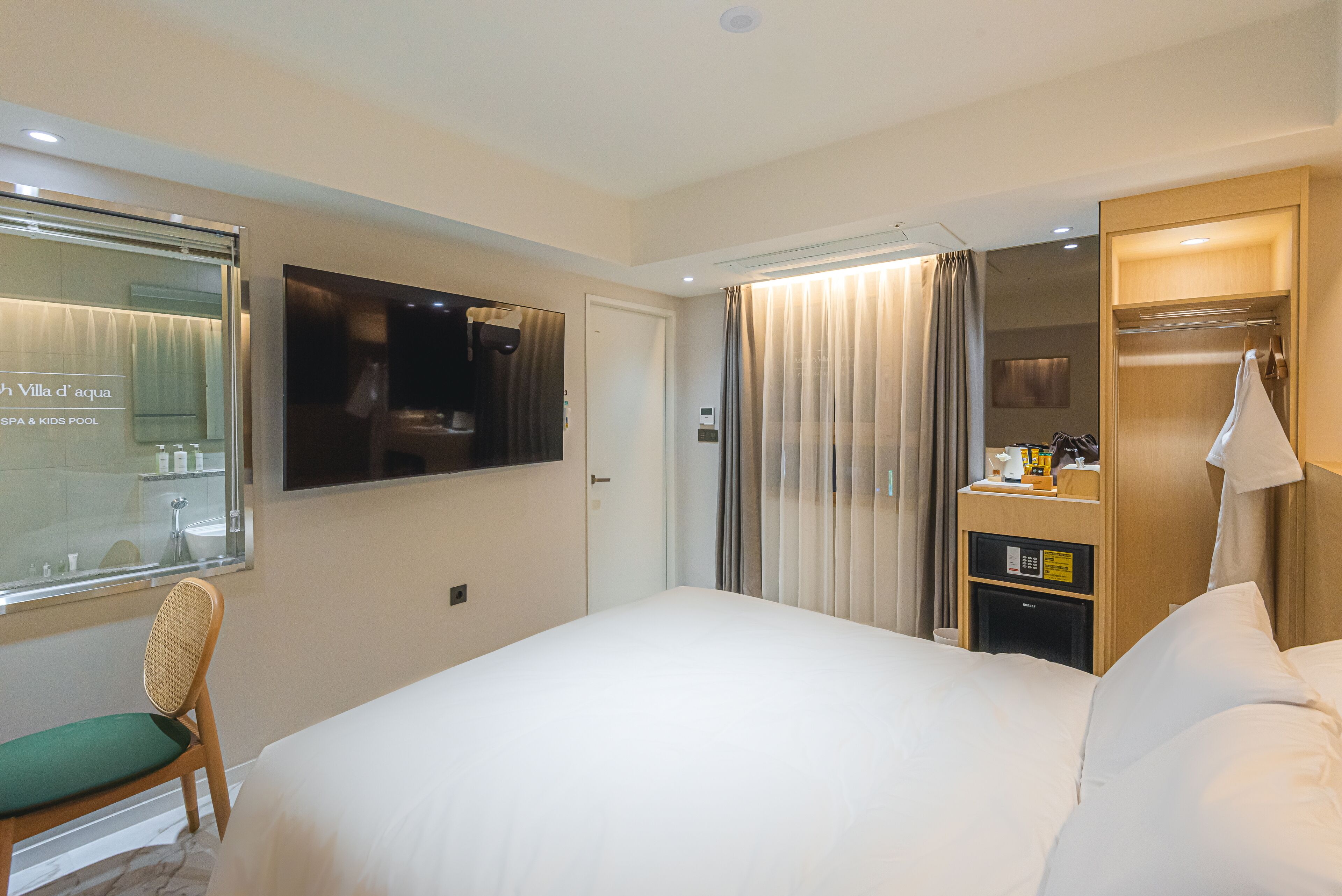 Quarto de hotel com cama, poltrona, televisão, espelho, armário e minibar.
