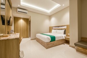 Quarto de hotel moderno com cama de madeira, uma pequena mesa de cabeceira, um banco embutido, televisão de tela plana e luminária no teto.