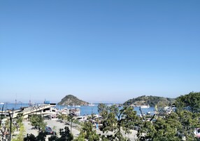 Marina costeira com barcos atracados, um passeio para pedestres e uma paisagem acidentada ao fundo.