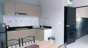 Uma cozinha com fogão, pia e armários, uma mesa de jantar com cadeiras e uma porta preta.