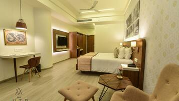 Quarto de hotel com cama, escrivaninha, cadeira e uma pequena mesa com abajur.