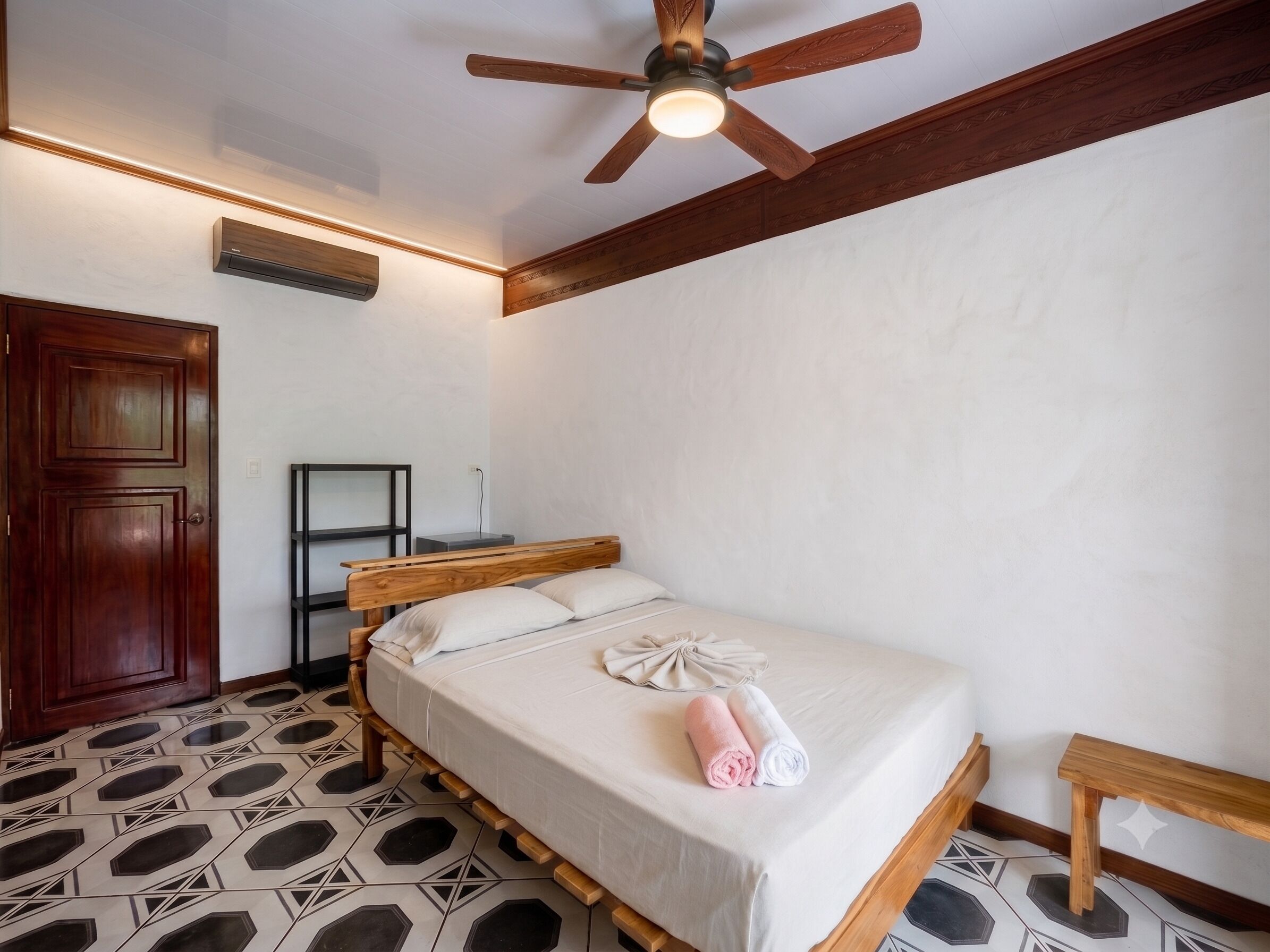 Um quarto com cama de madeira, ventilador de teto, porta de madeira e piso estampado.