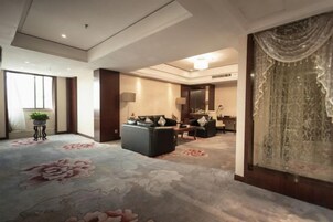 Um hall de hotel com piso coberto por carpete, área de estar com sofás, um espelho grande e uma cortina decorativa.