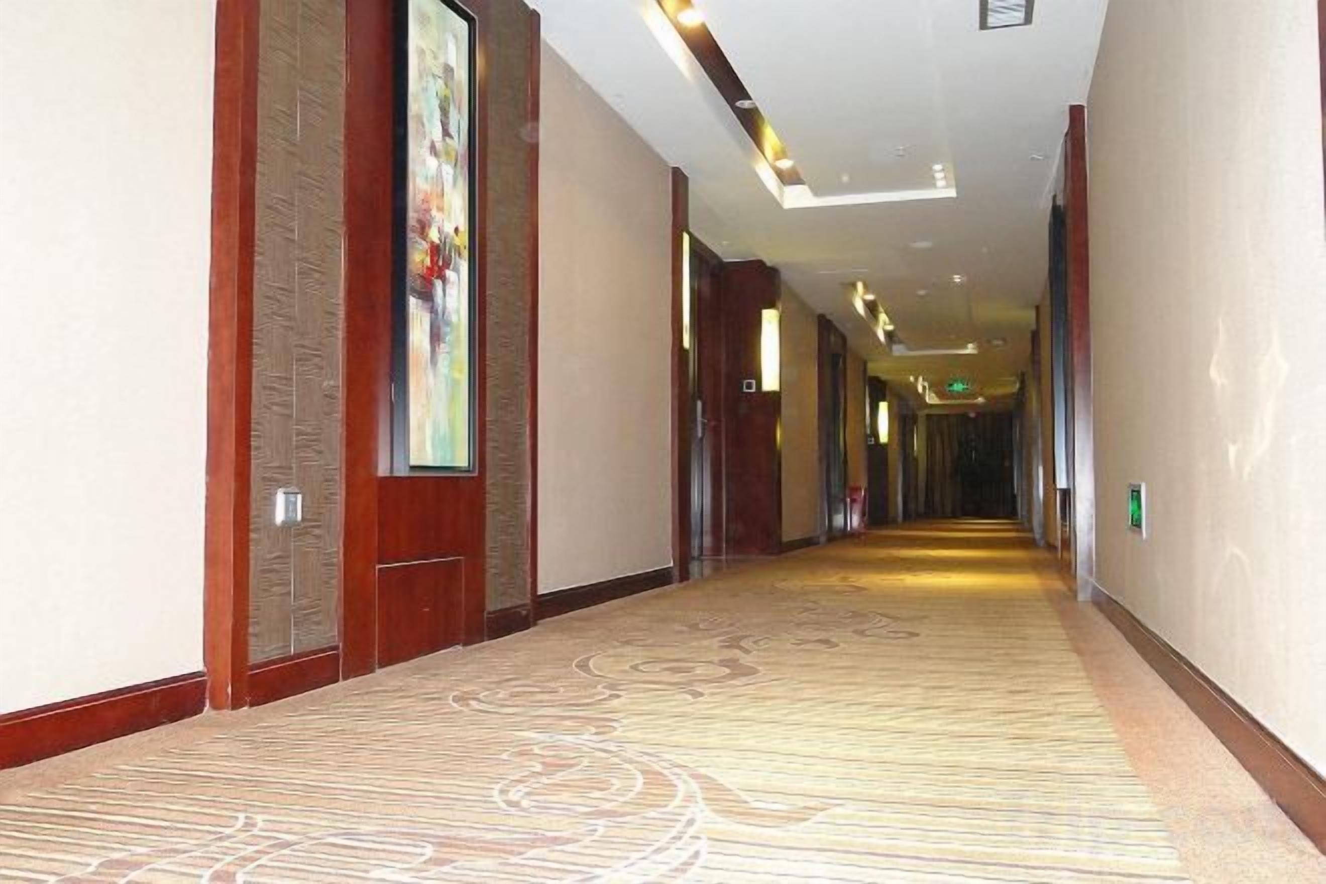 Corredor de hotel com carpete estampado, portas de madeira e um longo vão.
