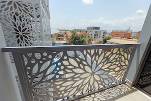 Uma varanda com grade metálica decorativa e vista para edifícios ao fundo.