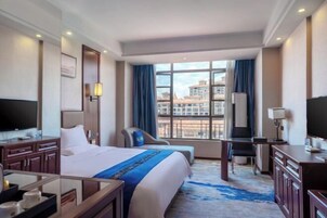 Quarto de hotel com uma cama grande, uma escrivaninha, uma cadeira e uma televisão.