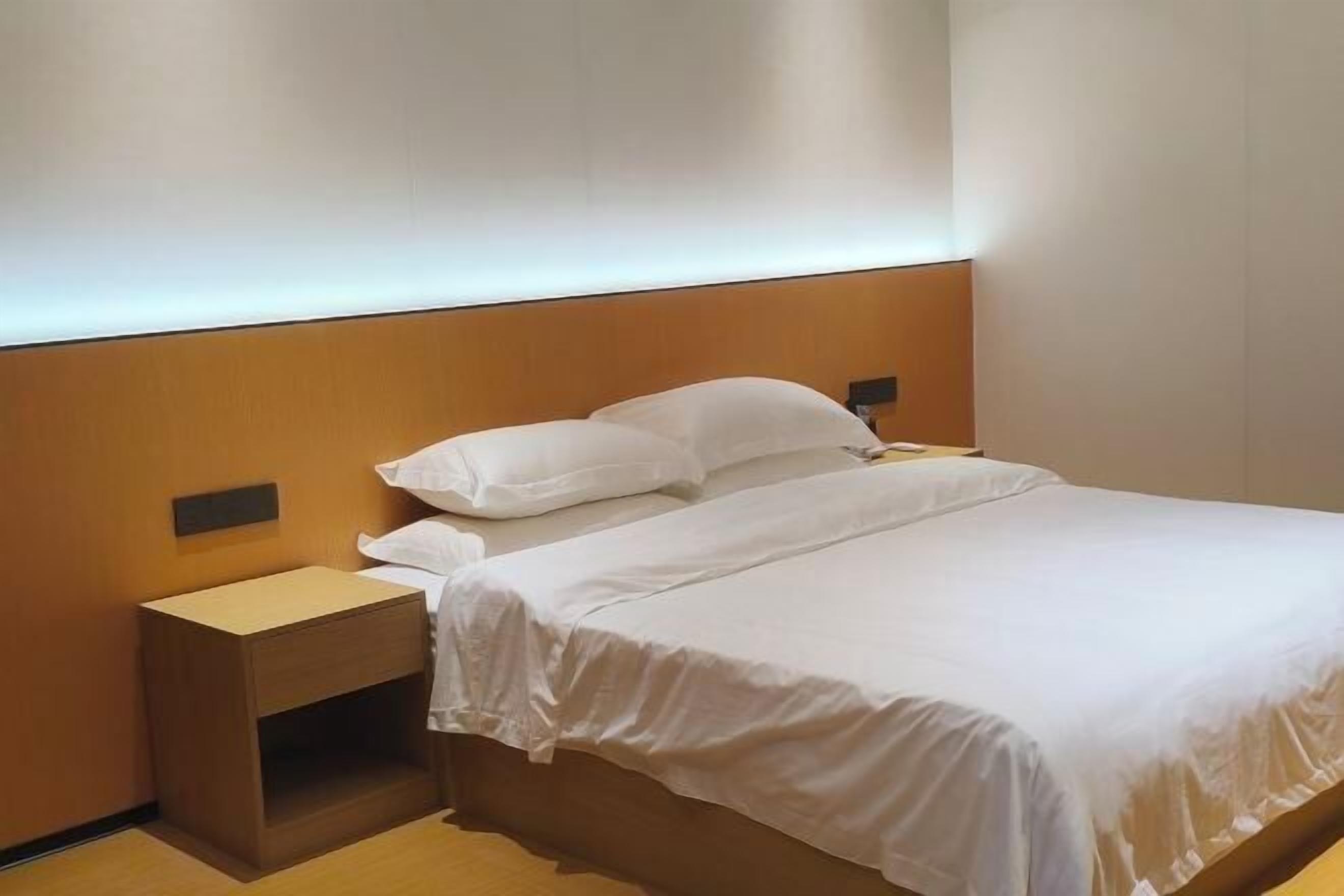 Quarto de hotel com uma cama de solteiro, uma mesa de cabeceira e uma cabeceira de madeira.