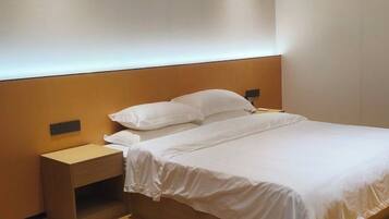 Quarto de hotel com uma cama de solteiro, uma mesa de cabeceira e uma cabeceira de madeira.