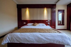 Quarto de hotel com uma cama grande, cabeceira com listras verticais e uma janela com cortinas.