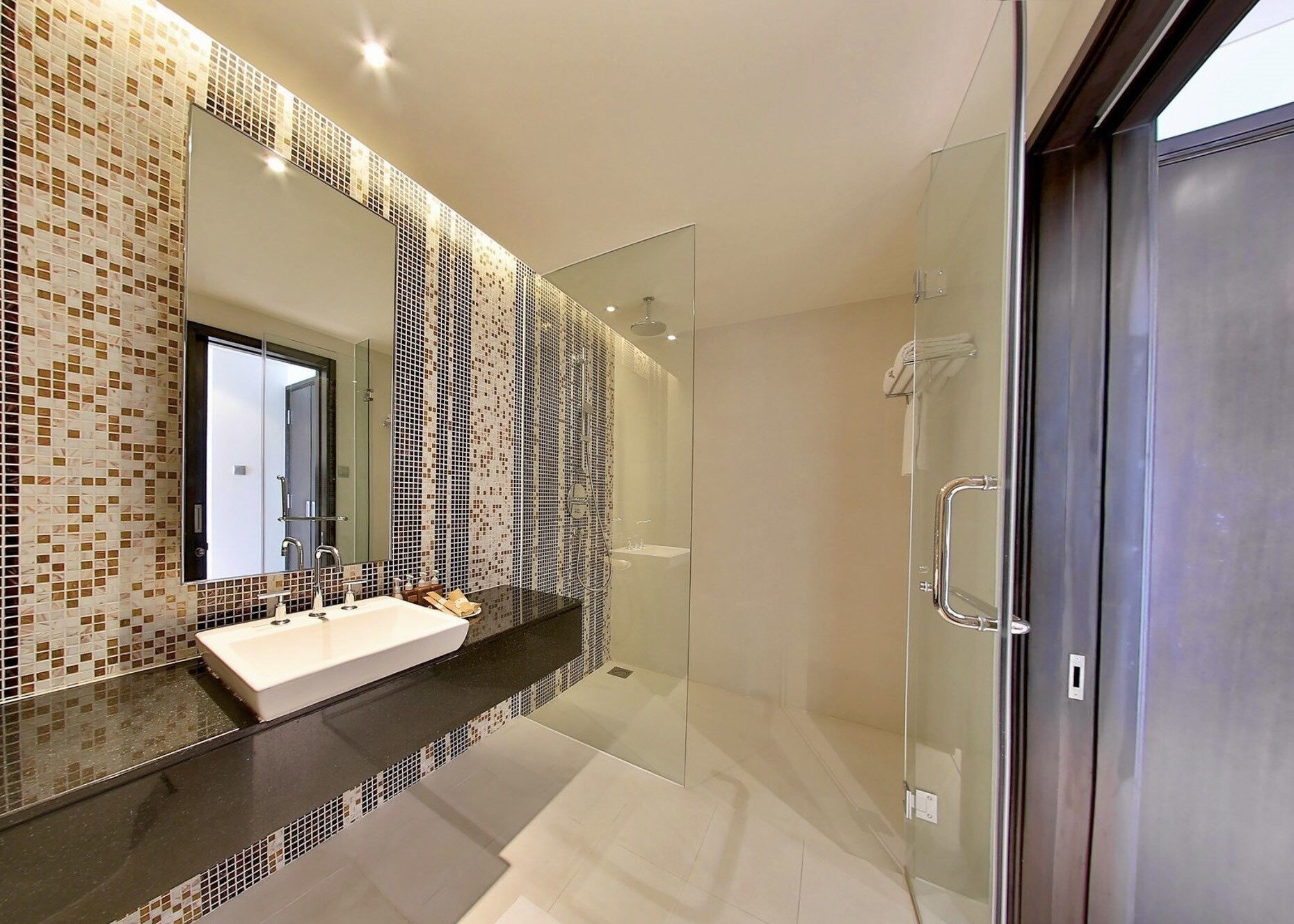 Um banheiro moderno com box de vidro, um espelho grande e painel de azulejos.