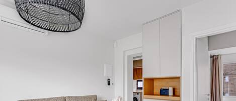 Uma sala de estar moderna com um sofá, uma mesa de centro com um vaso, e uma cozinha ao fundo.