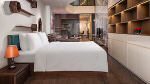 Quarto de hotel moderno com cama grande, área de estar, espaço para refeições e interior bem iluminado.