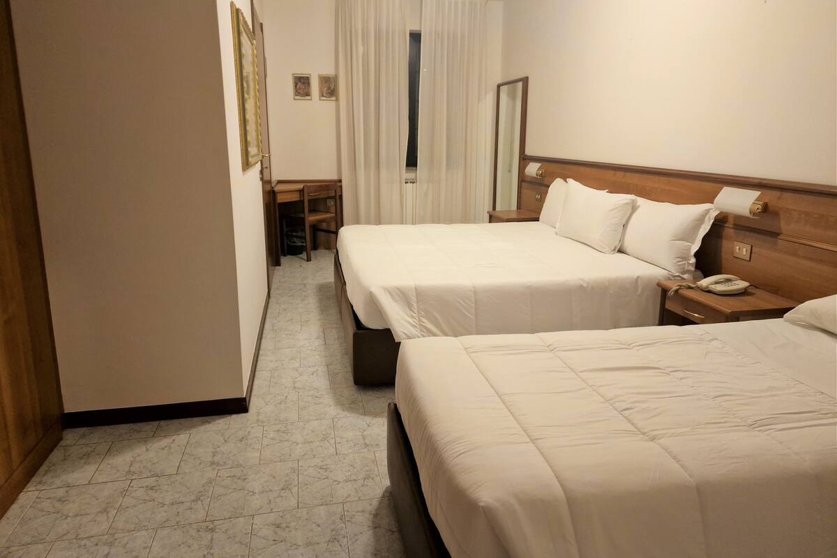 Quarto de hotel com duas camas, uma mesa, uma cadeira e banheiro.