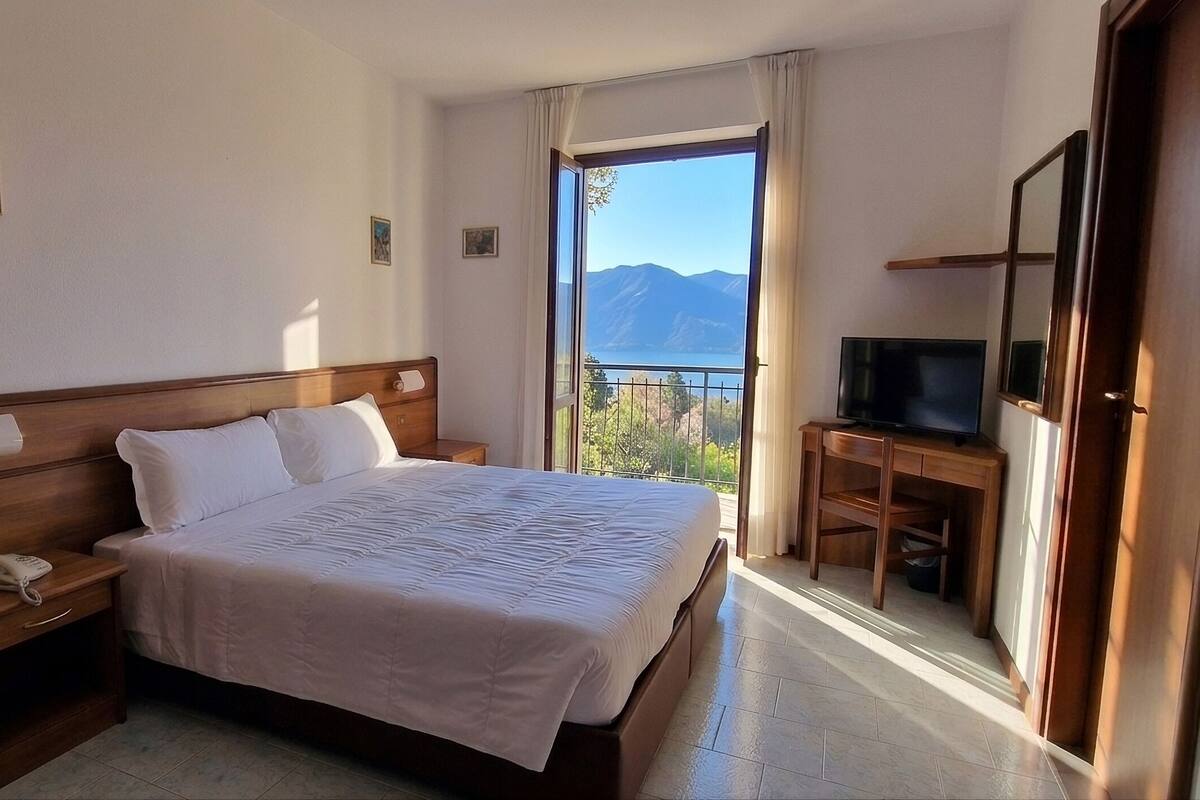 Quarto de hotel com cama, telefone ao lado da cama, suporte para TV e varanda com vista para as montanhas.