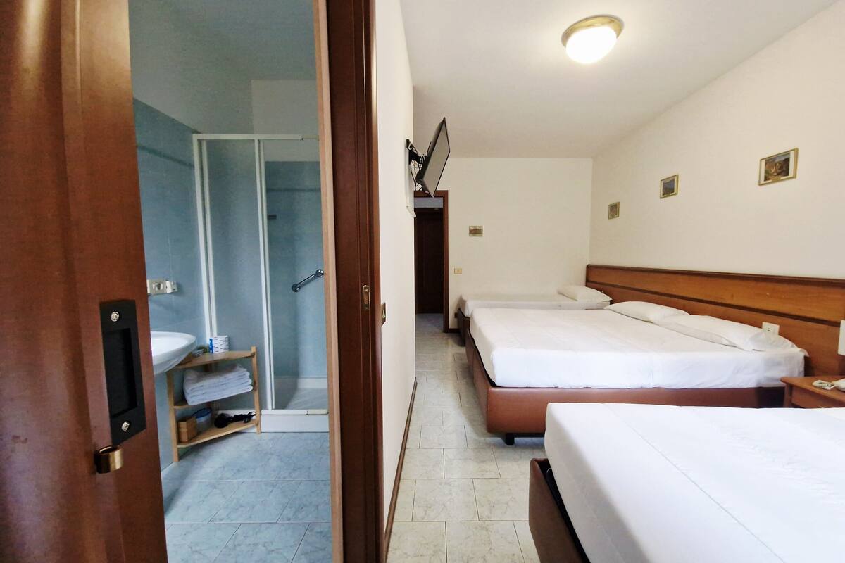 Quarto de hotel com duas camas, banheiro com chuveiro e porta de madeira.