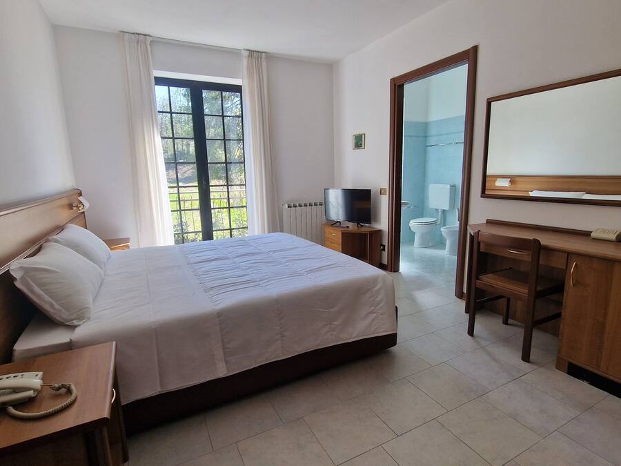 Quarto de hotel com cama, secretária com telefone, televisão e banheiro visível por uma porta aberta.